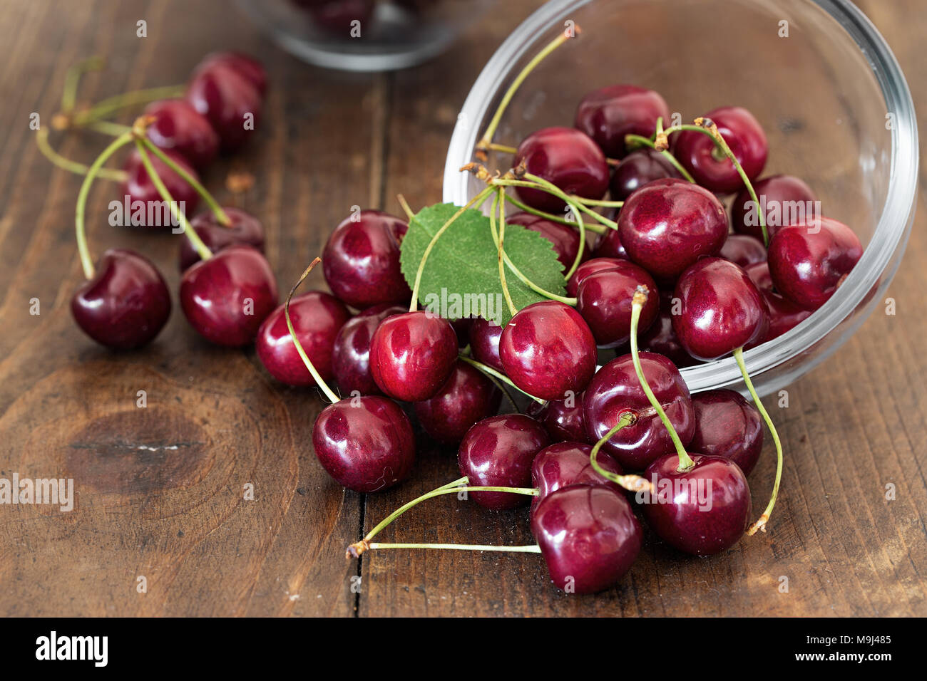Sweet cherries scattered on a brown wooden table from a glass plate ...