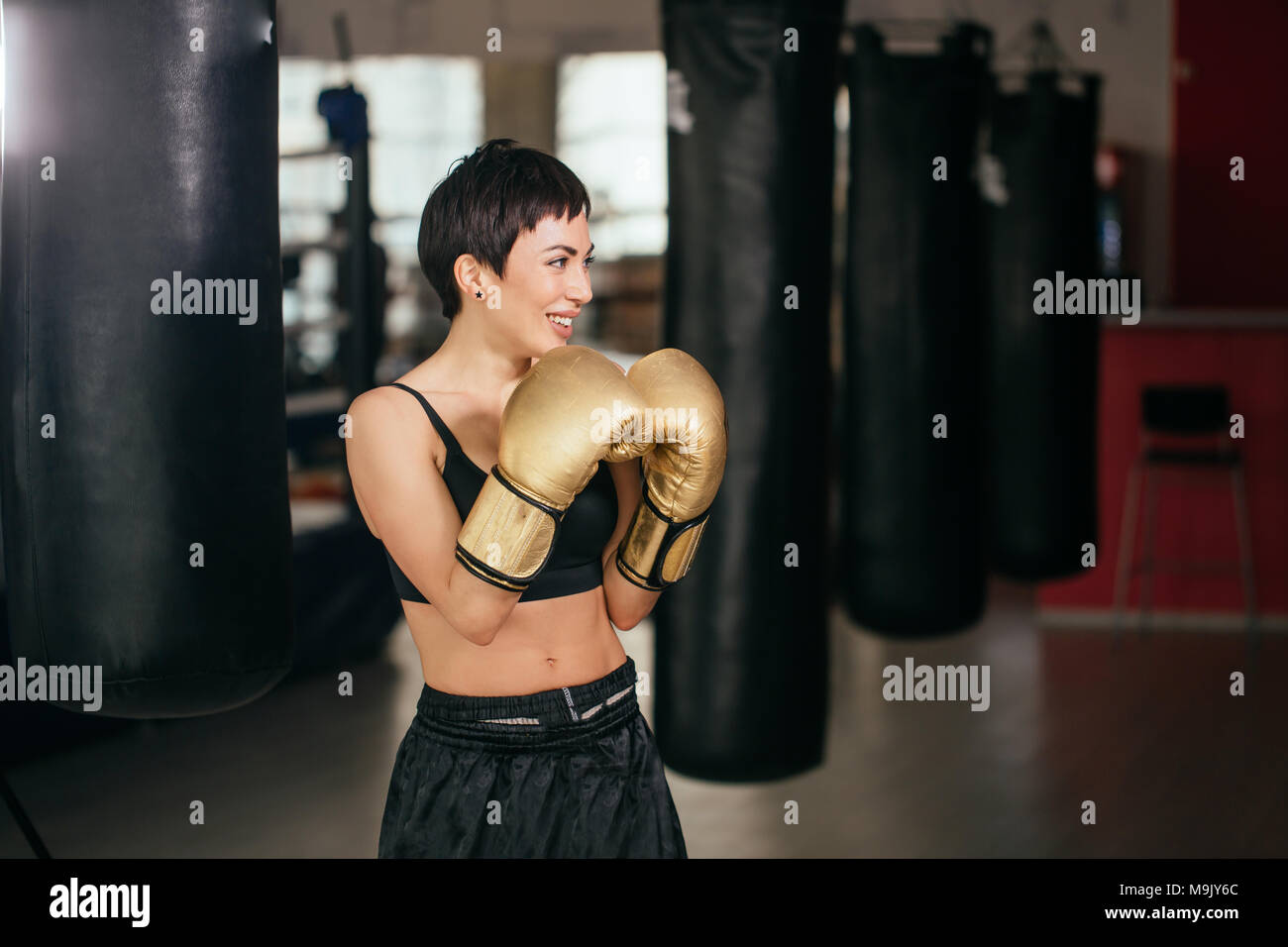 side view image of smiling woman in black sporty suit showing boxing ...