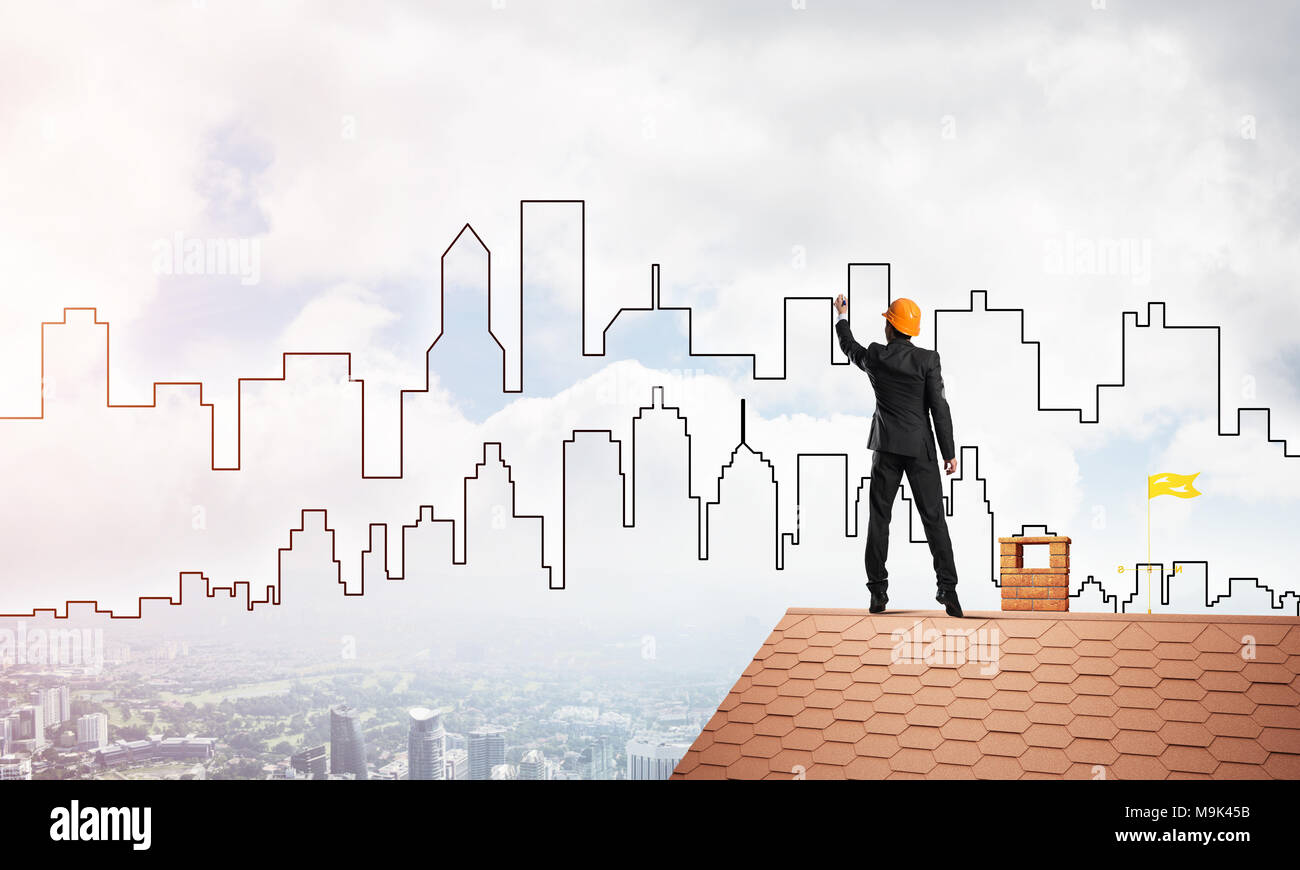 Engineer man standing with back on house roof and drawing city. Mixed ...