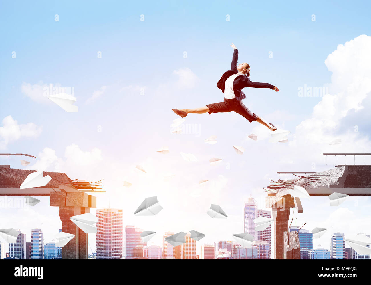 Business woman jumping over gap with flying paper planes in concrete ...