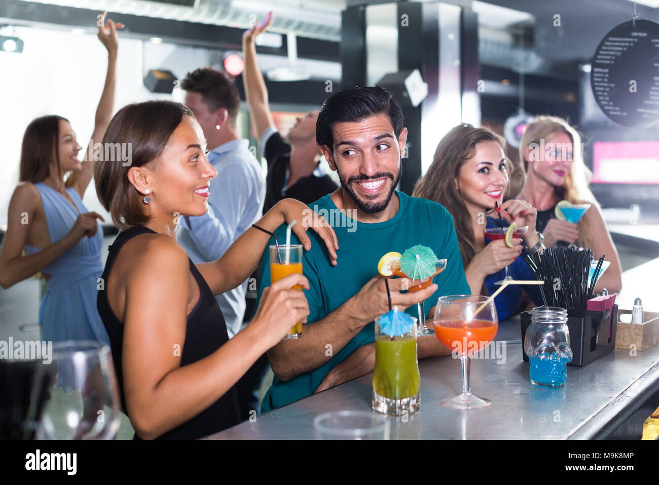 adult joyous male with female are talking and drinking cocktails on the ...