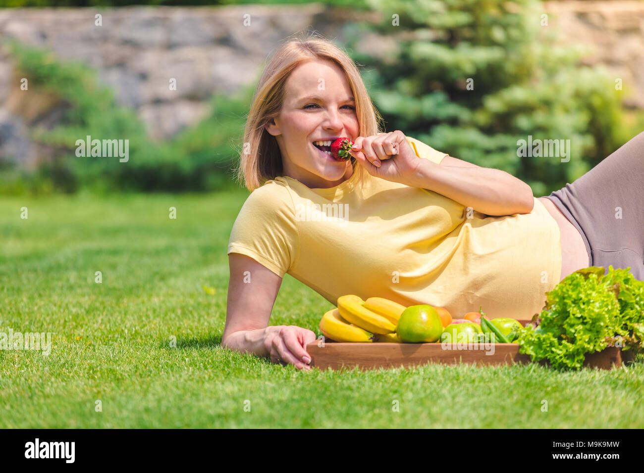 Pregnant woman lies on grass and eats fresh fruit Stock Photo - Alamy