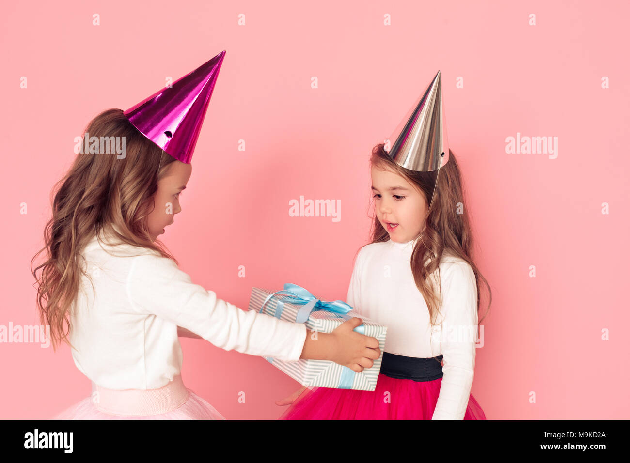 Two little children girls celebrating birthday studio isolated on pink ...