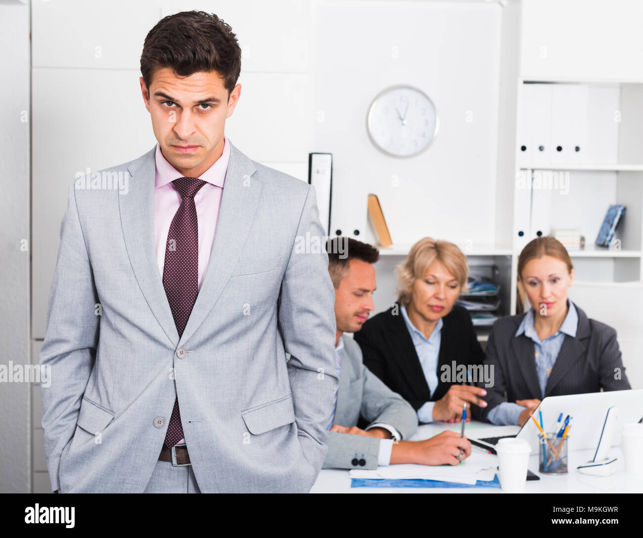 Unhappy and tired man standing at office on background with working colleagues Stock Photo - Alamy