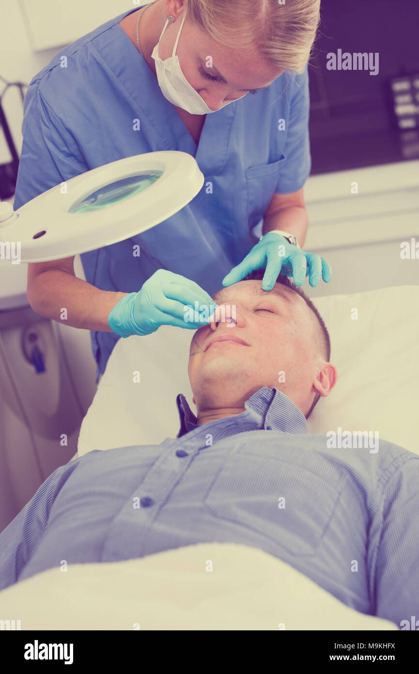 Woman specialist is cleaning skin of patient with using magnification ...