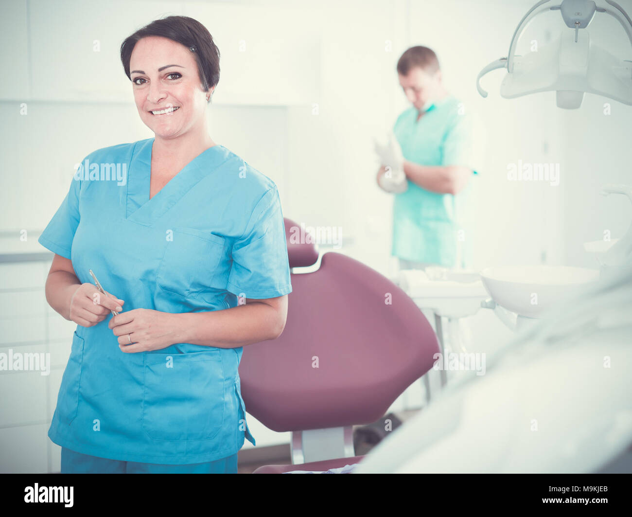 Portrait of adult smiling dentist in medical center with assistant ...