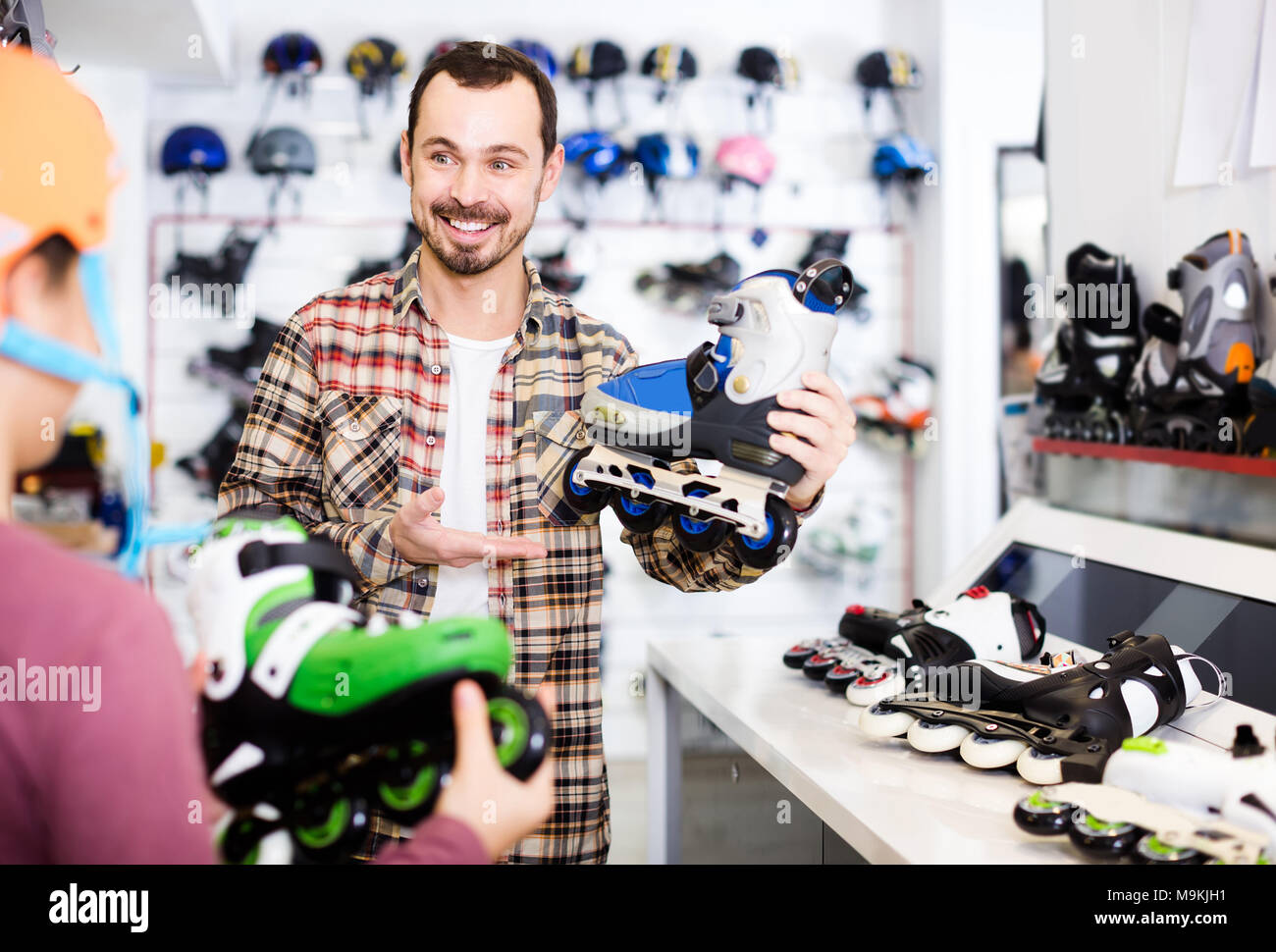 smiling european male shop assistant helping boy to choose roller ...