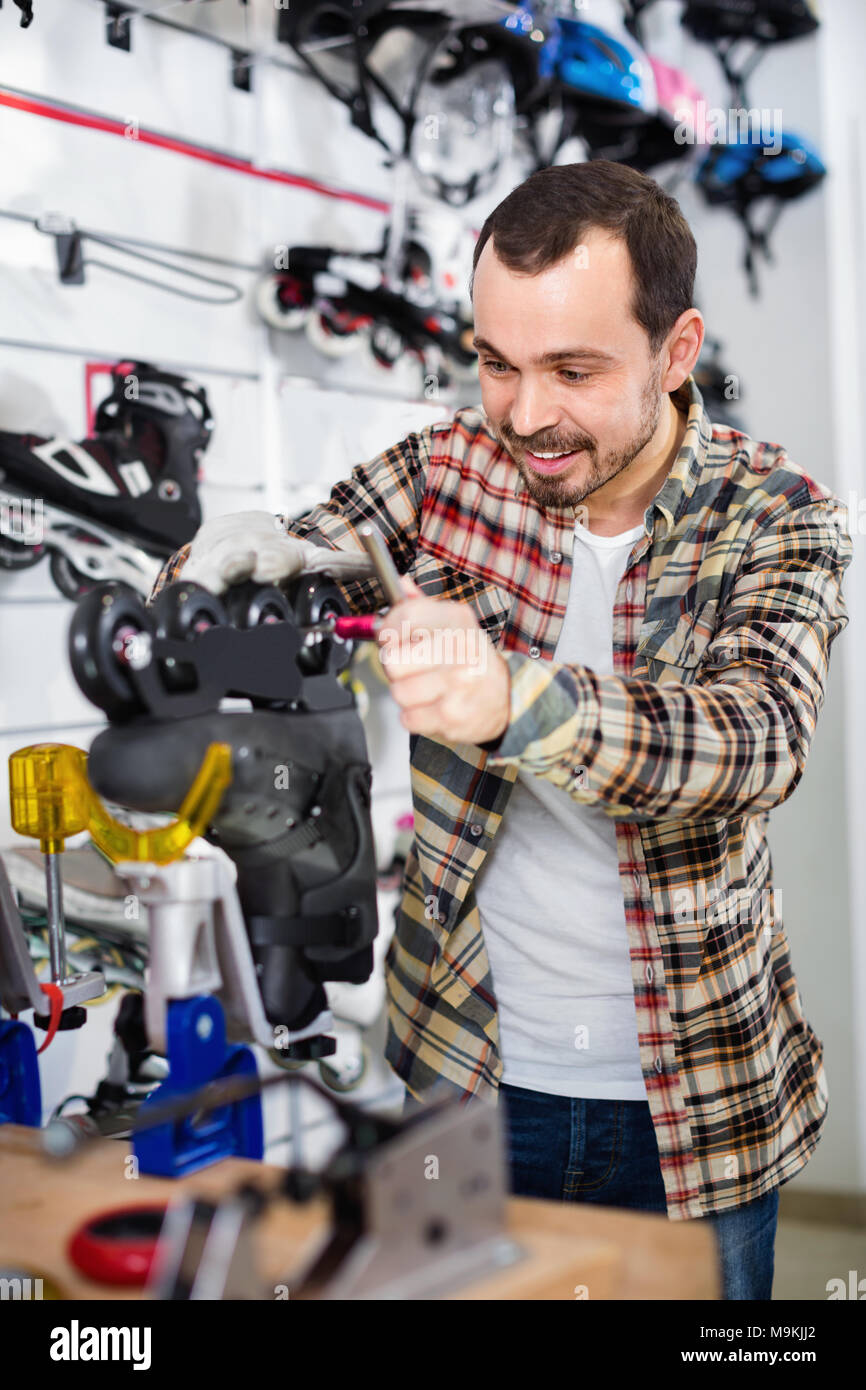 Satisfied pleasant smiling male master fixing roller-skates in sports ...