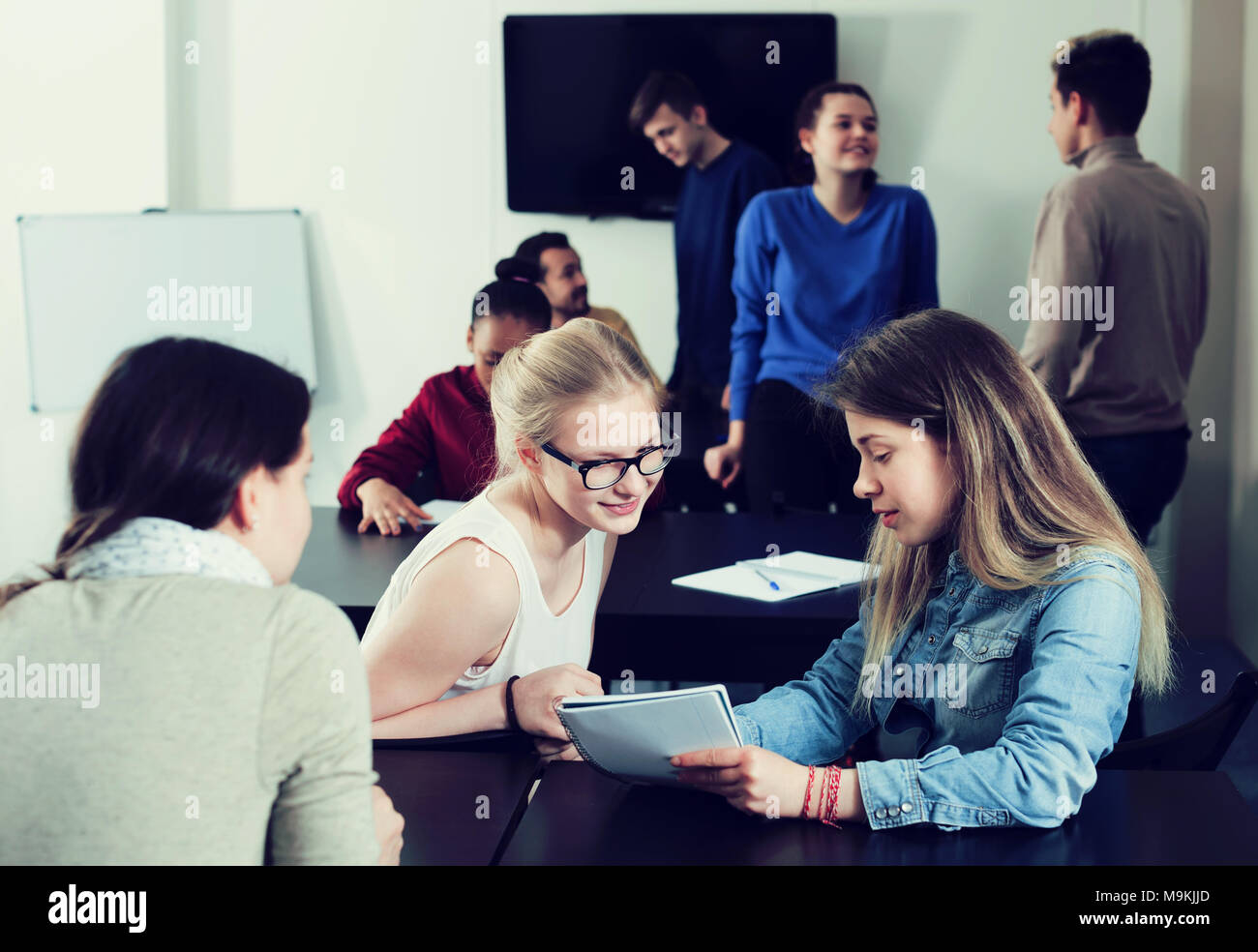 Young girl consulting fellow student during test examination in class ...