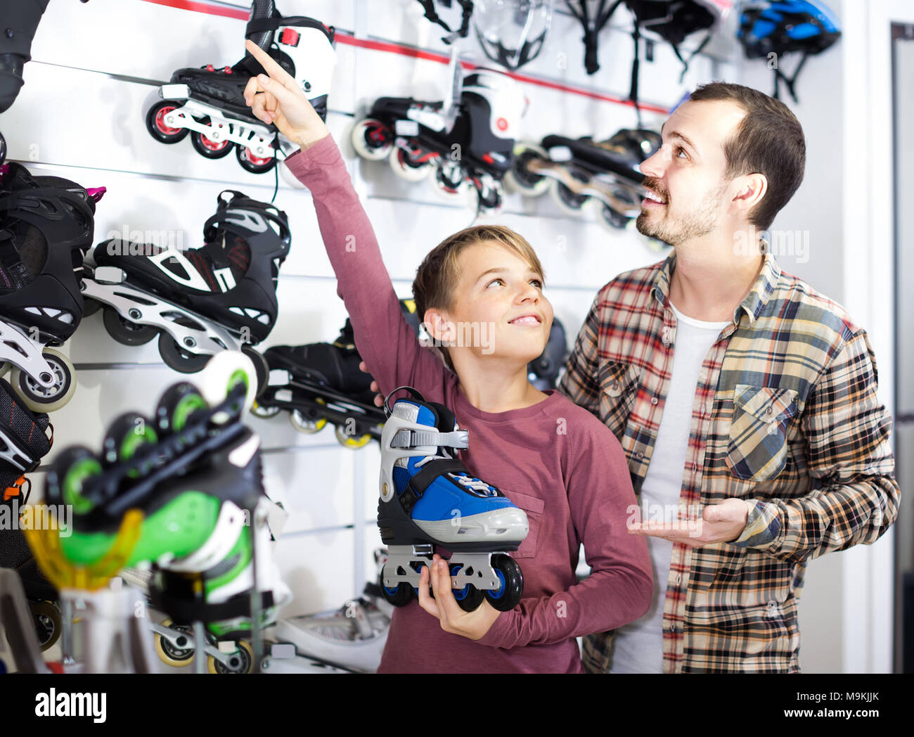 happy male shop assistant helping boy to choose roller-skates in sports ...