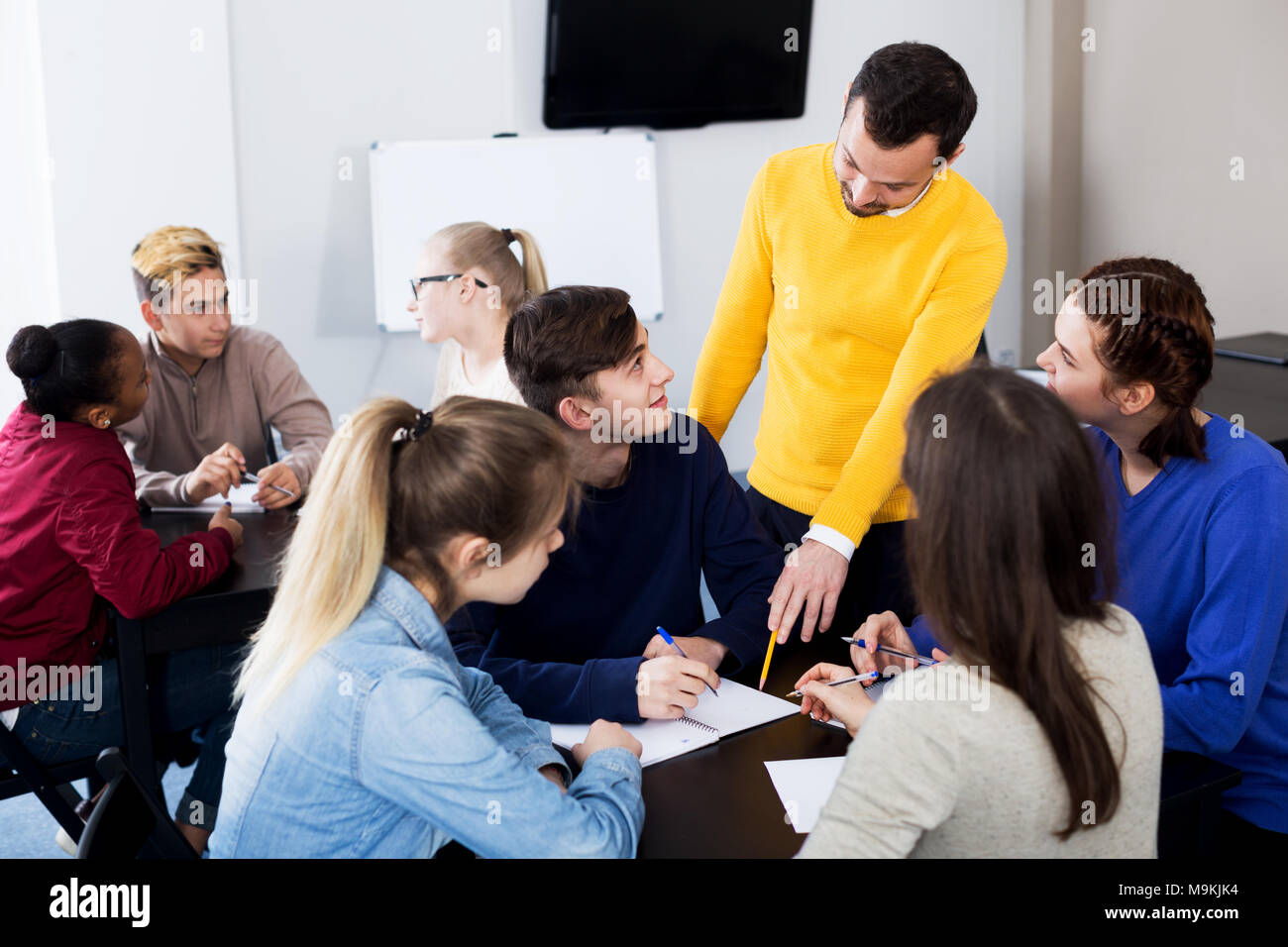 Positive classmates and male teacher working in groups to complete task ...
