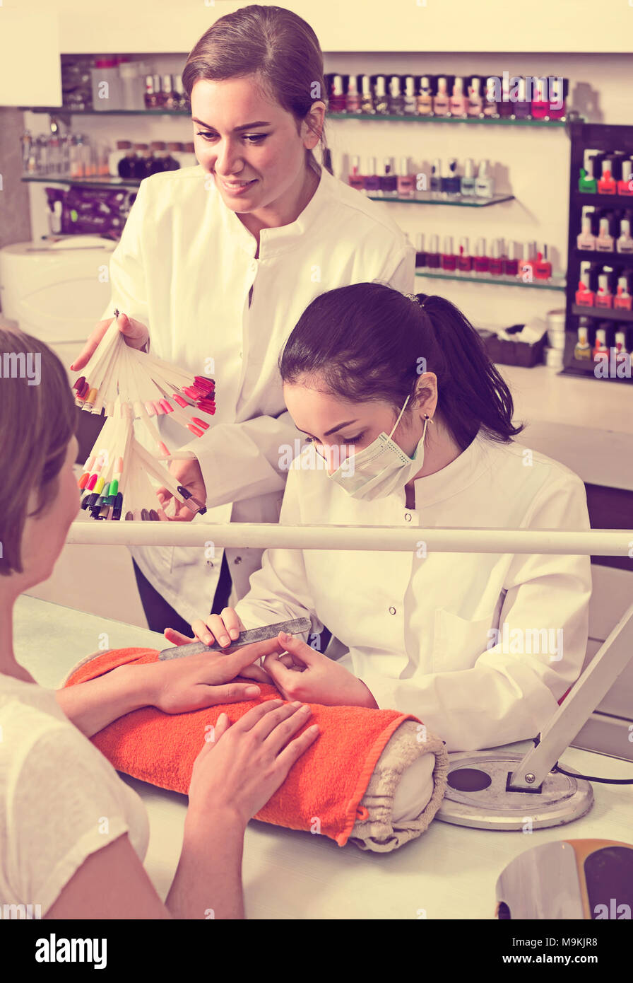 happy european manicurists choosing color of nail polish with client in ...