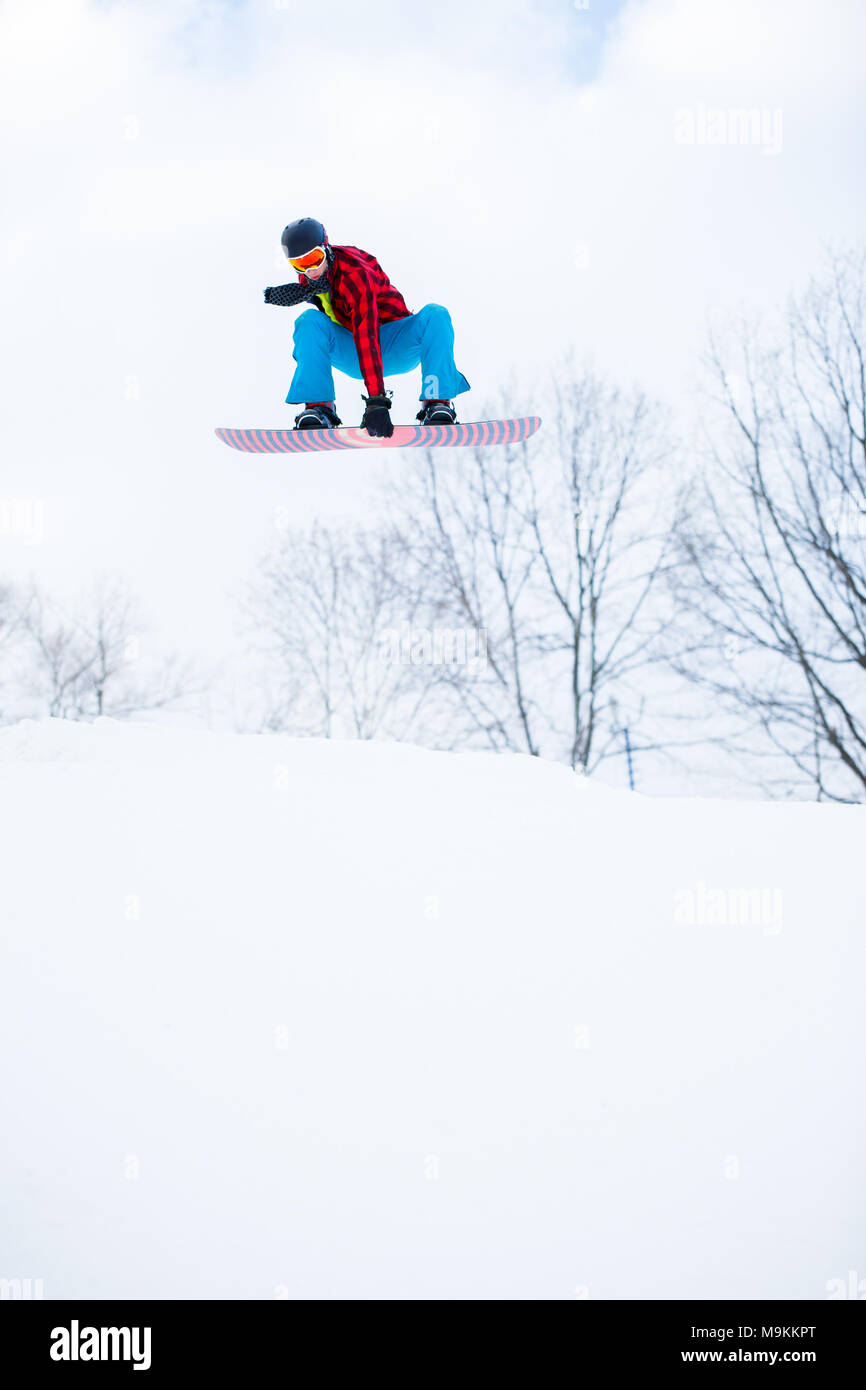 Image of athlete wearing helmet with snowboard jumping in snowy resort ...