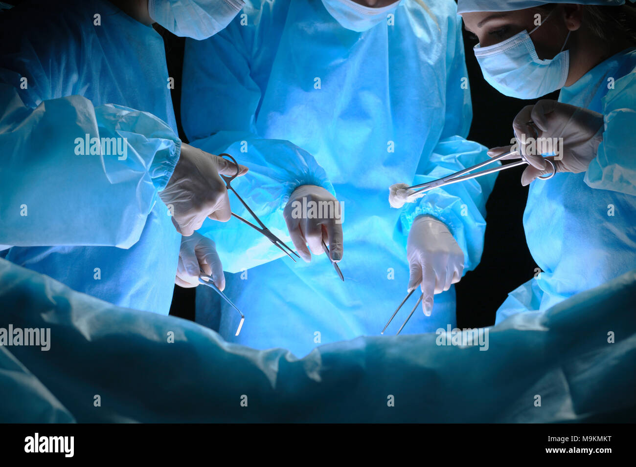 Group of surgeons at work in operating theater toned in blue. Medical ...