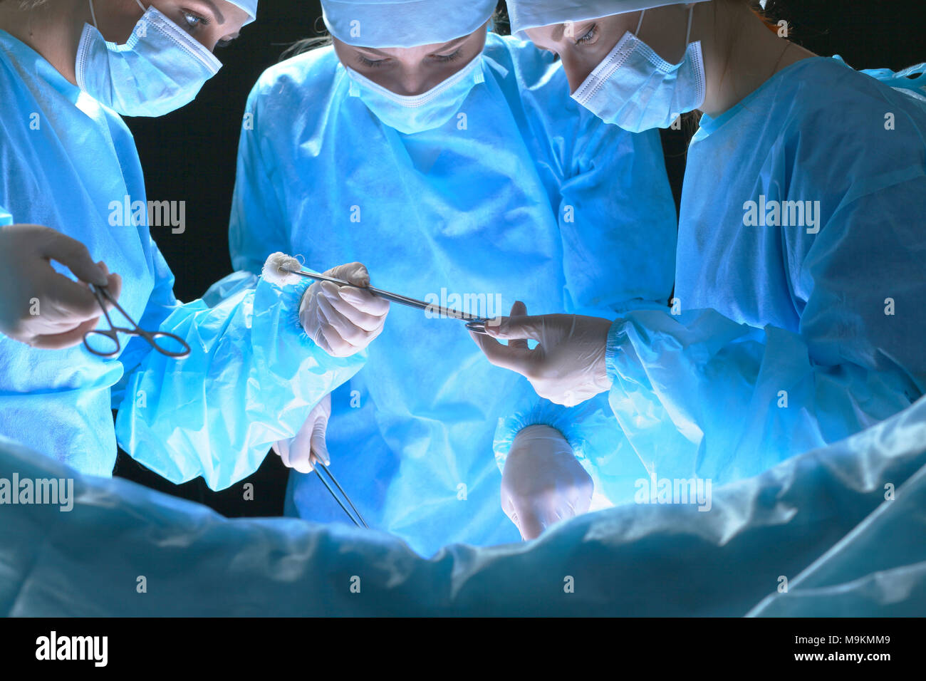Group of surgeons at work in operating theater toned in blue. Medical ...