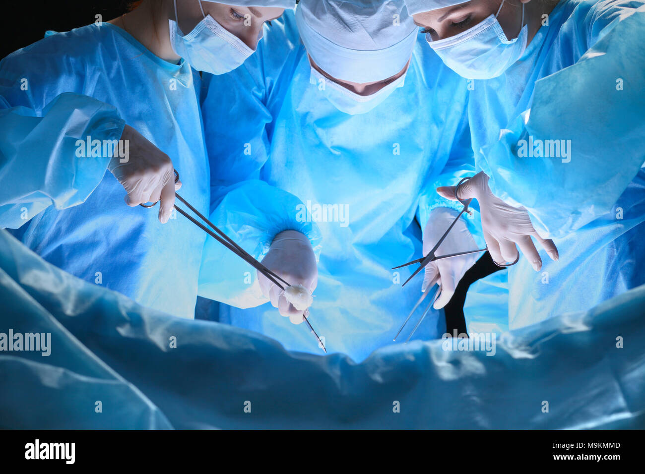 Group of surgeons at work in operating theater toned in blue. Medical ...