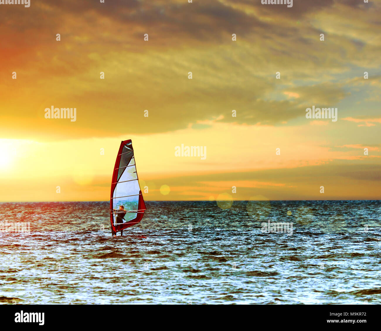 Windsurfer in the sea with a scenic sunset sky. Toned, lens sun flare ...