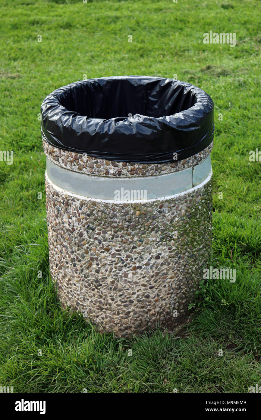 Concrete litter bin containing a black plastic bin liner with grass ...