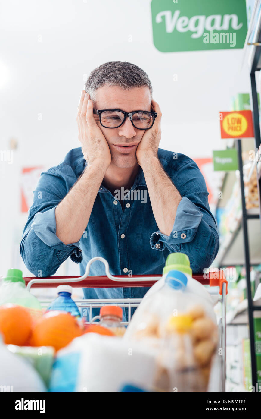 Sad exhausted man shopping at the supermarket, he is leaning on the ...
