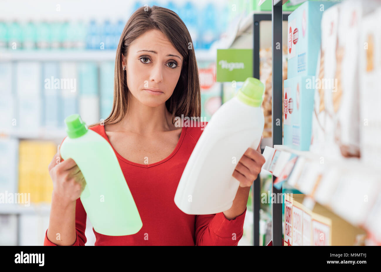 Woman shopping at the supermarket and comparing detergent products, she ...