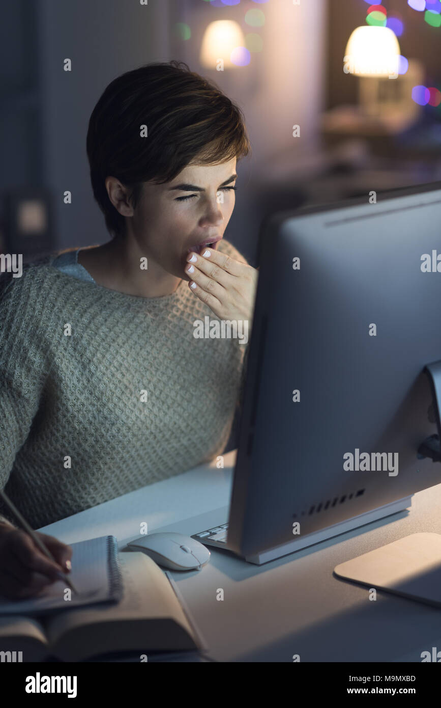 Young tired woman working with her computer late at night, she is ...