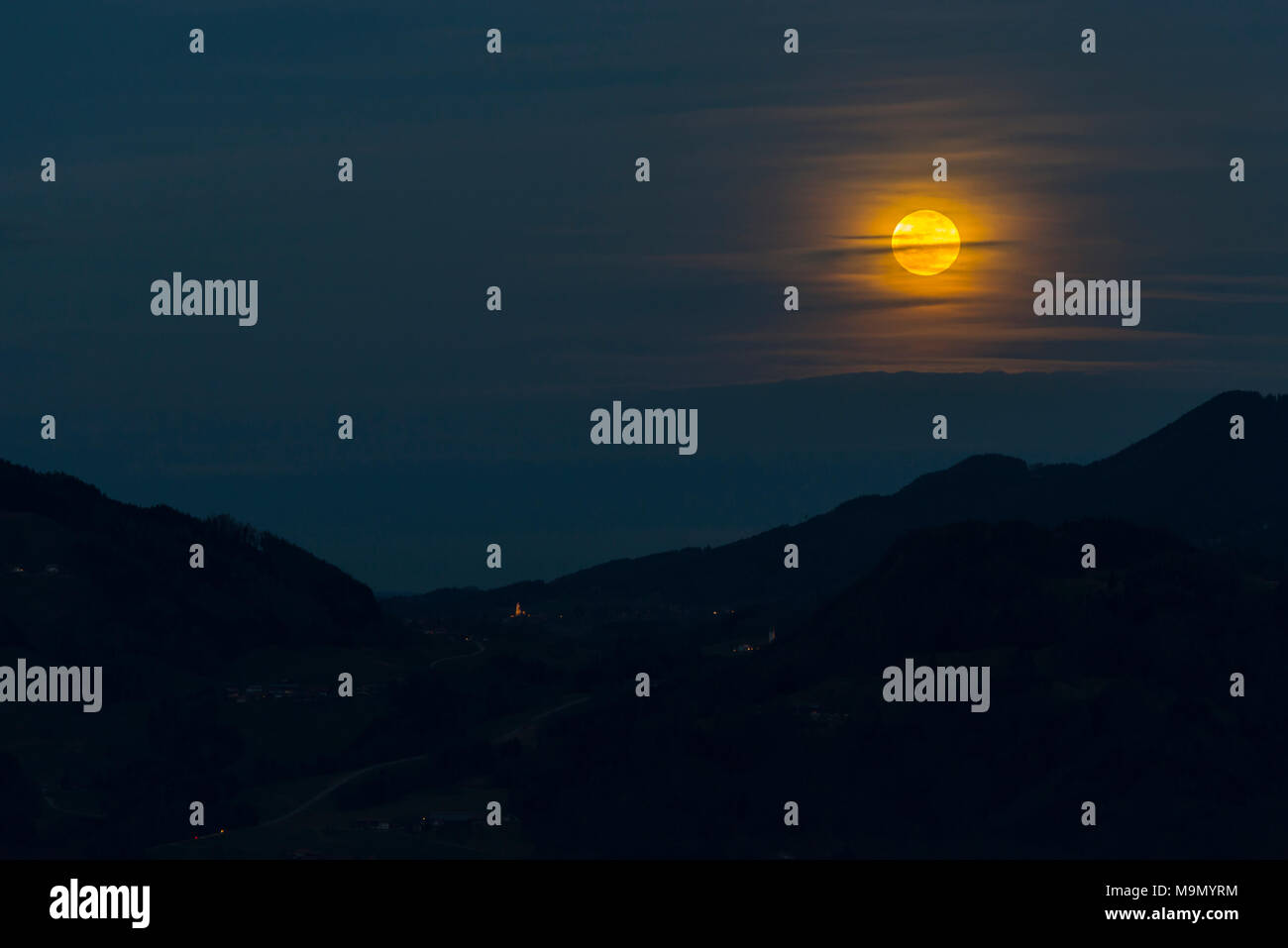 Super moon full moon rising golden in the night sky over rural alpine ...
