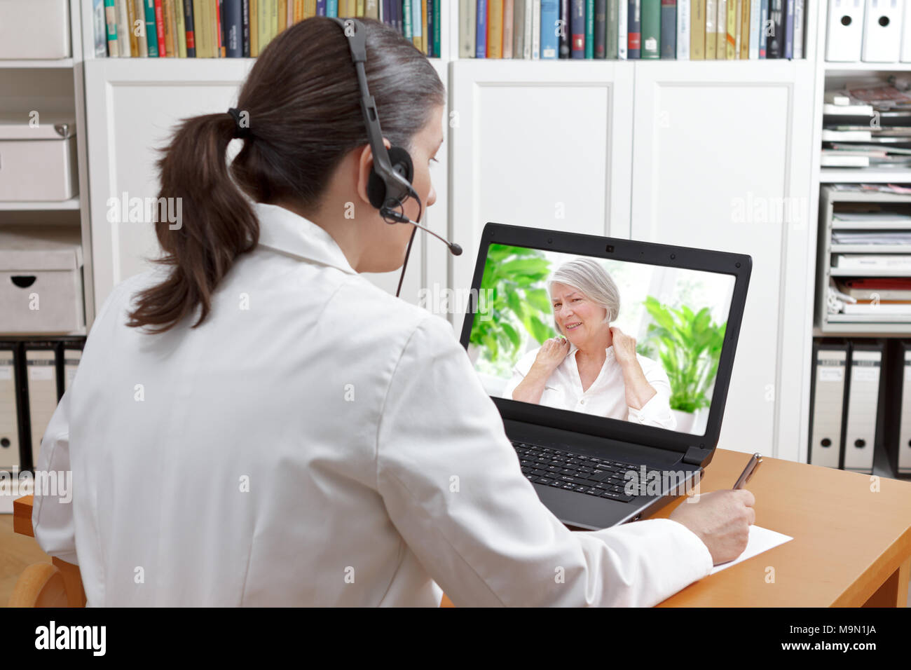 Doctor sitting at the desk of her office with headset and laptop ...