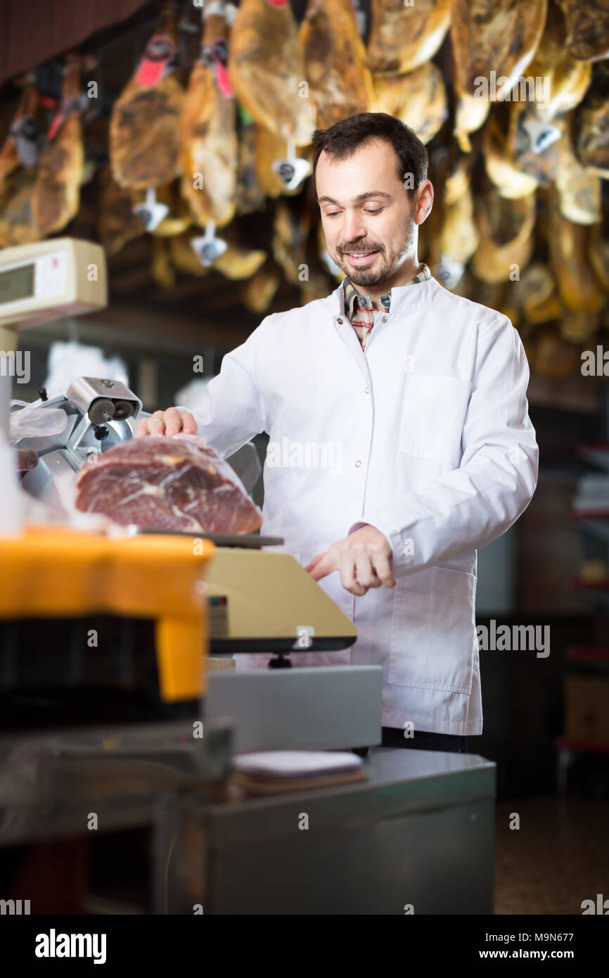 Smiling male butcher weighing on scales piece of meat in butcher’s ...