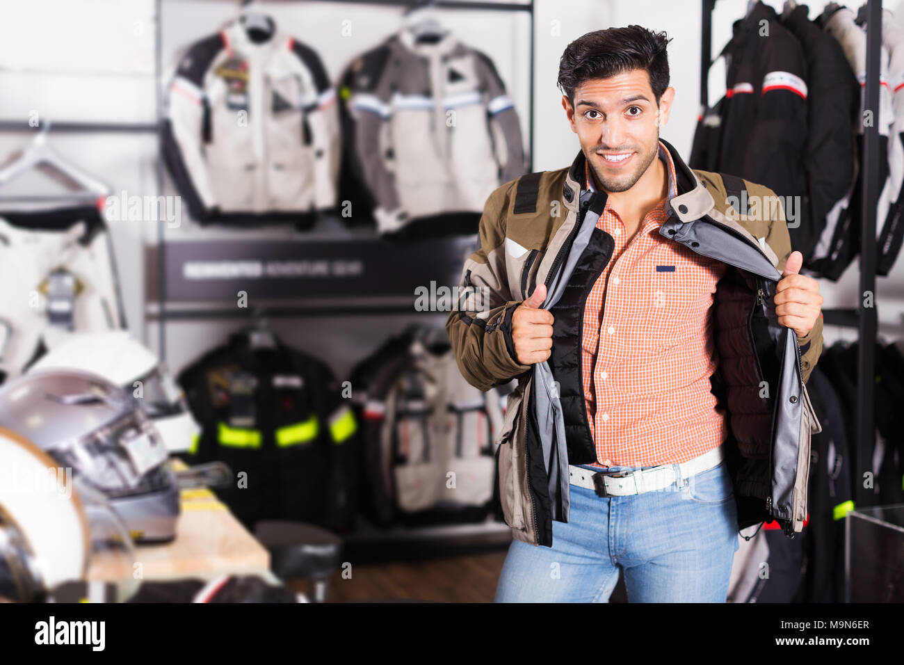 happy young male customer is trying up modern jacket in the sport store ...