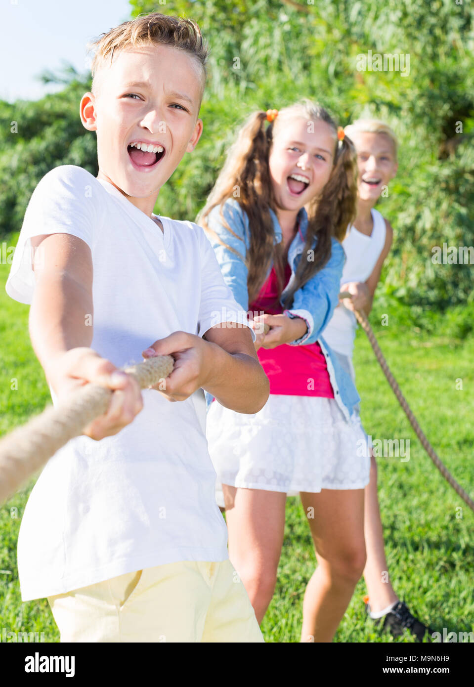Group of laughing children having fun together outdoors pulling rope ...