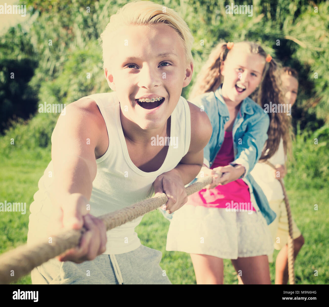 Group of laughing children having fun together outdoors pulling rope ...
