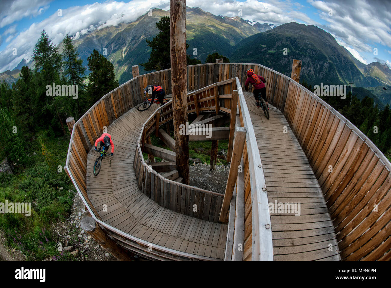 A group of mountain bikers ride a wooden feature on a trail in the ...
