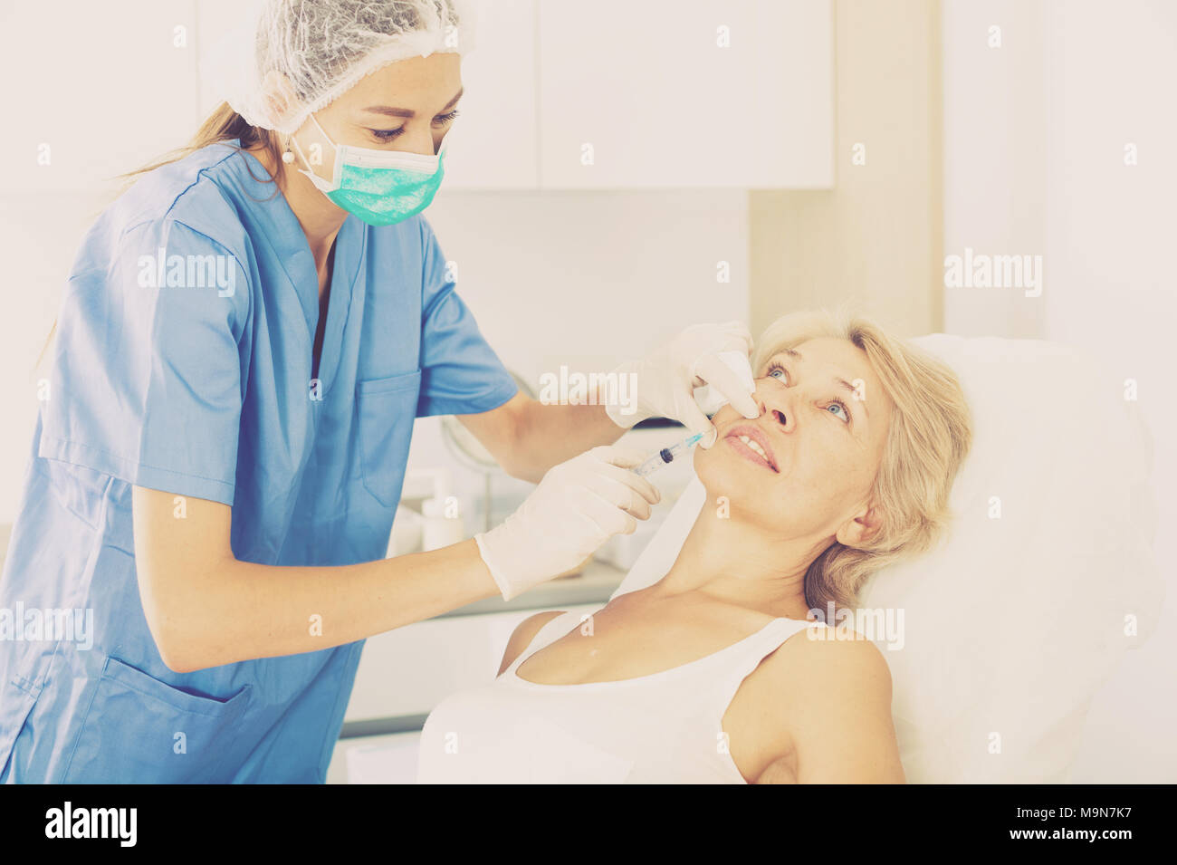 Mature female client receiving cosmetic injection from professional ...