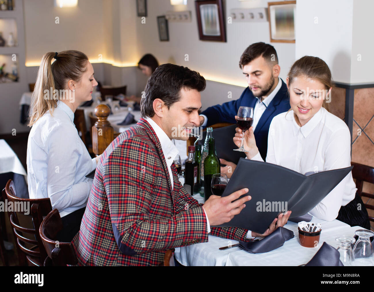 Glad positive smiling friends choosing dishes out of menu card in ...