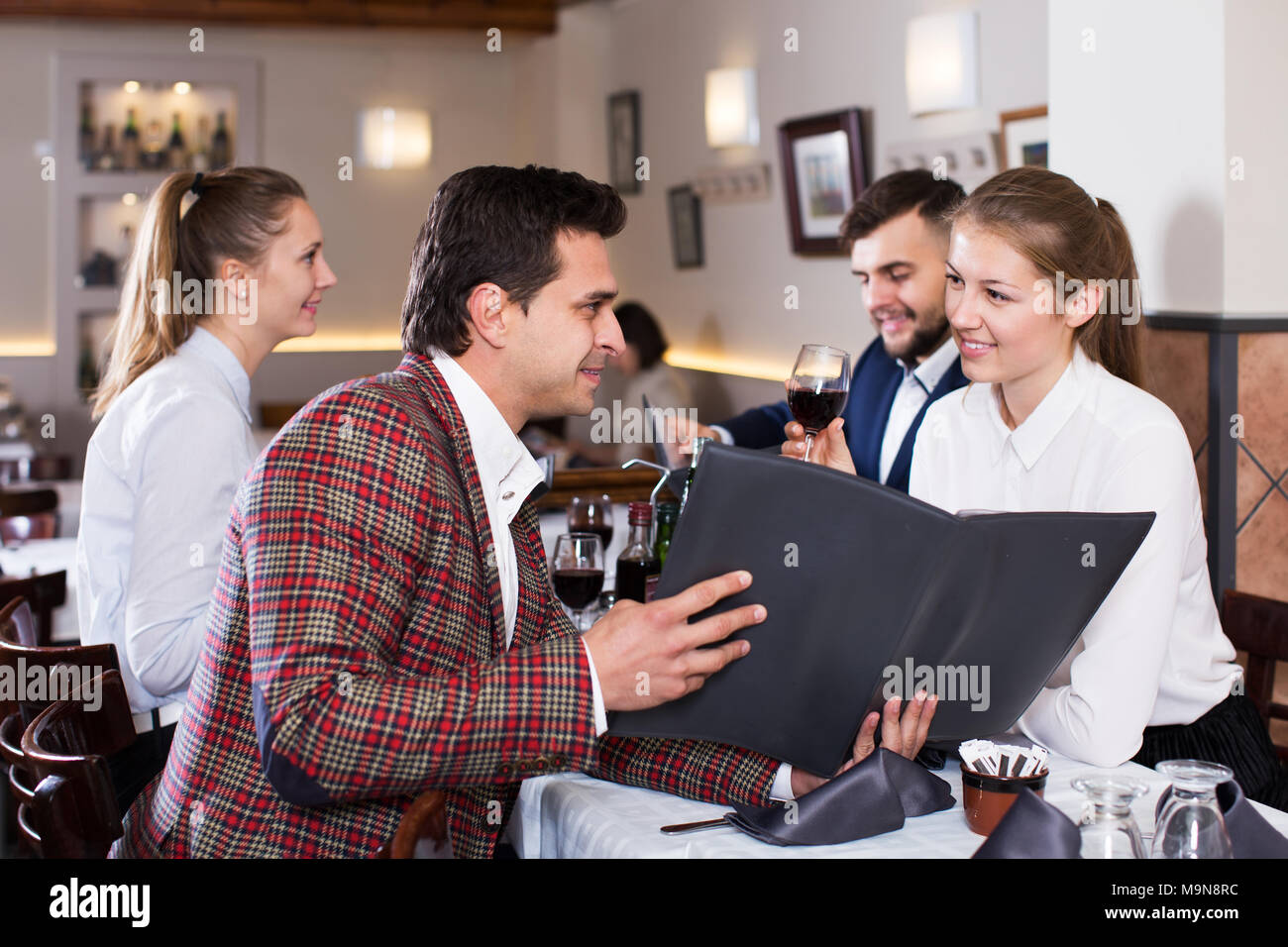 Group of glad friends enjoying dinner at restaurant, choosing meal from ...