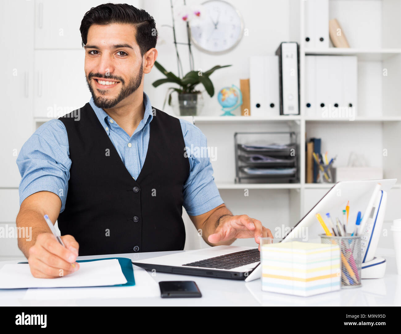 Smiling businessman is working behind laptop and reading documents in ...