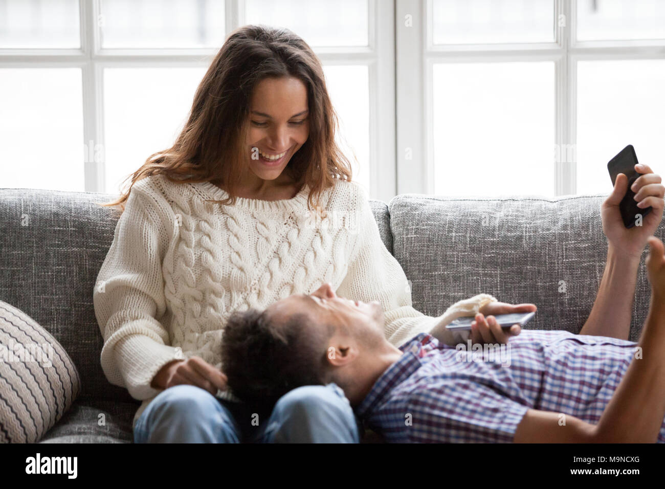 Happy smiling couple relaxing on sofa talking with smartphones in hands ...