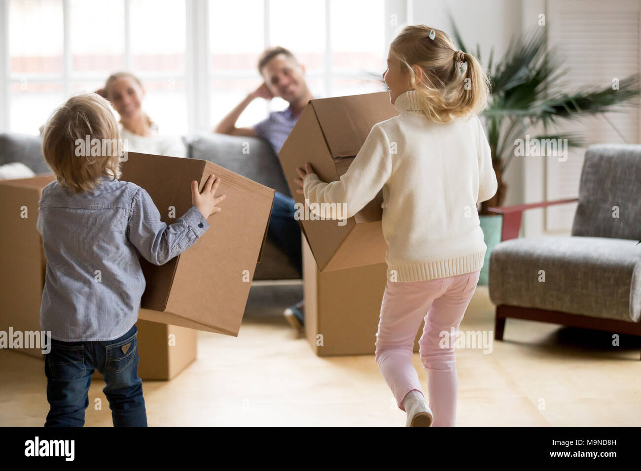 Rear view at kids playing with boxes on moving day, small brother and ...
