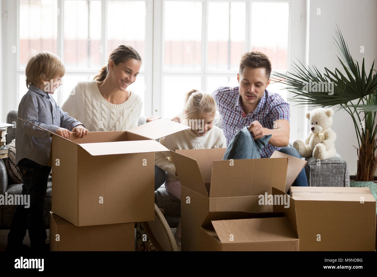 Young happy family with kids packing boxes on moving day together ...