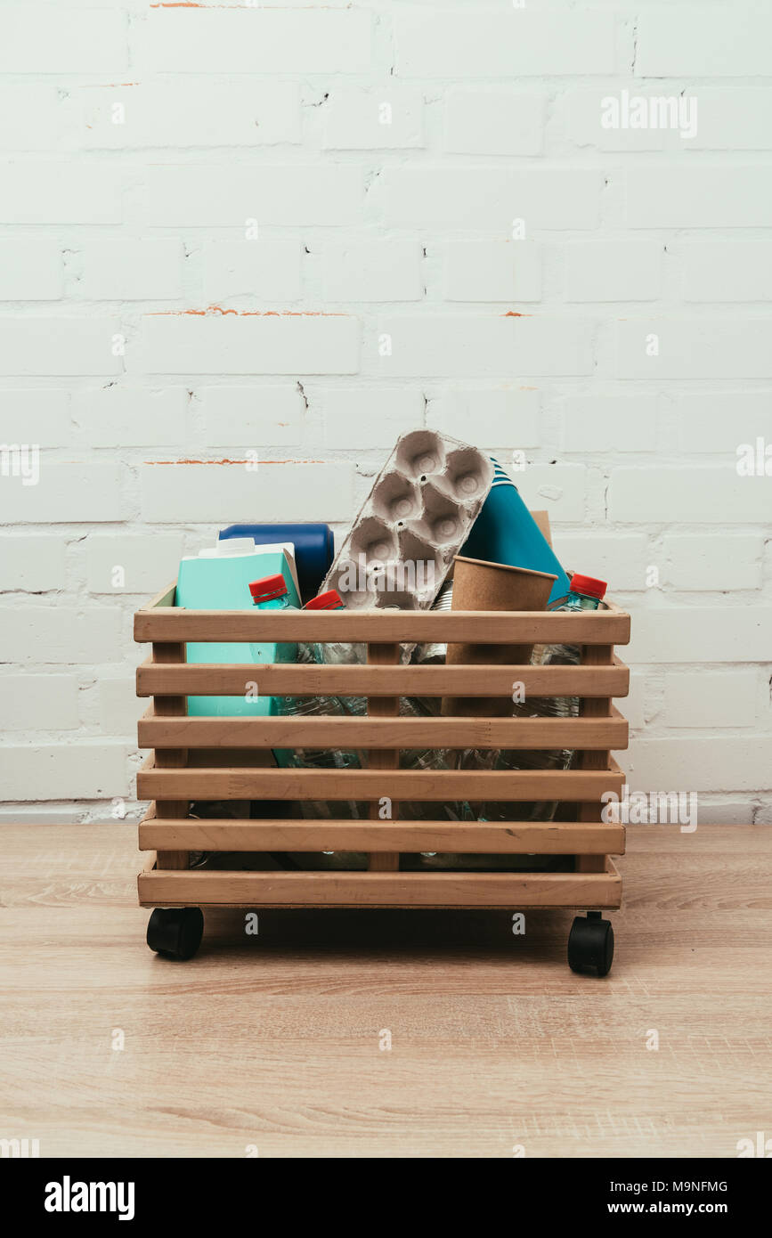 close up view of various types of trash in wooden box with white brick ...