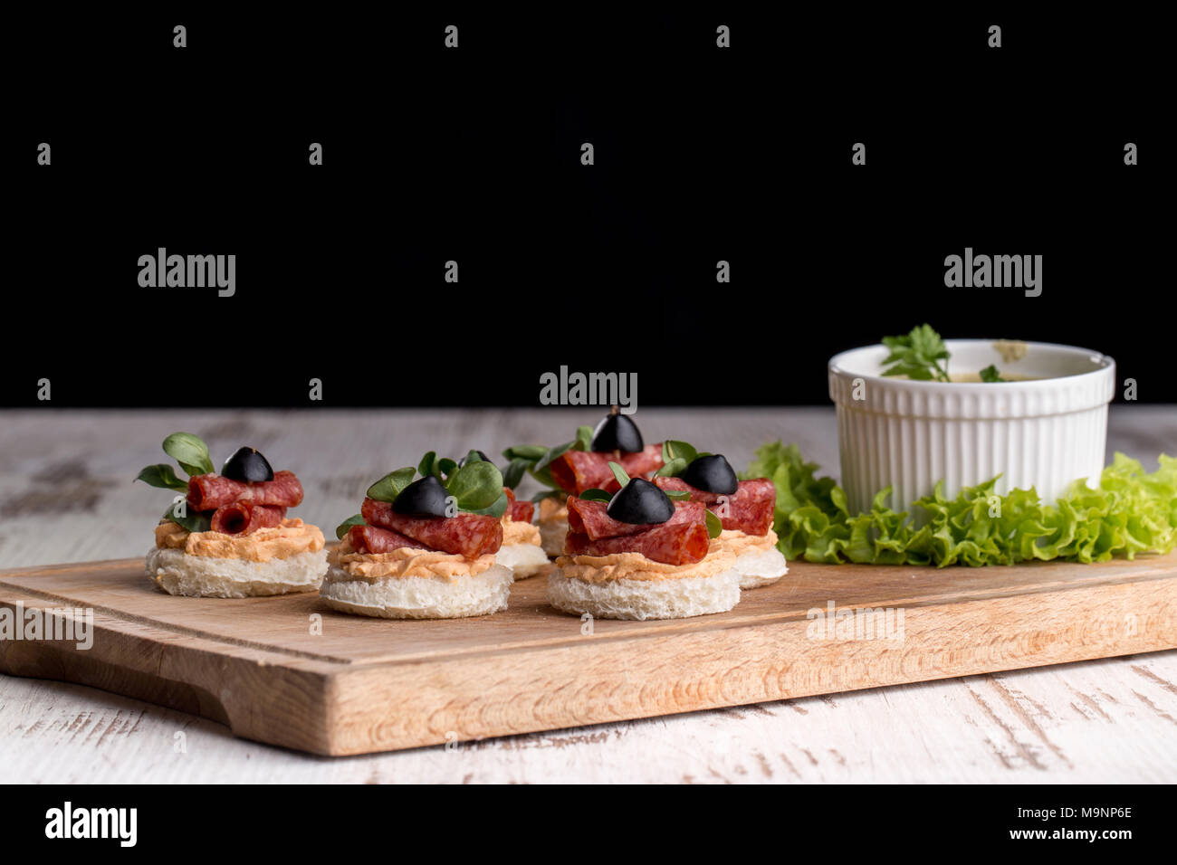Delicious canapes with salami, olives and spices on a woody background ...