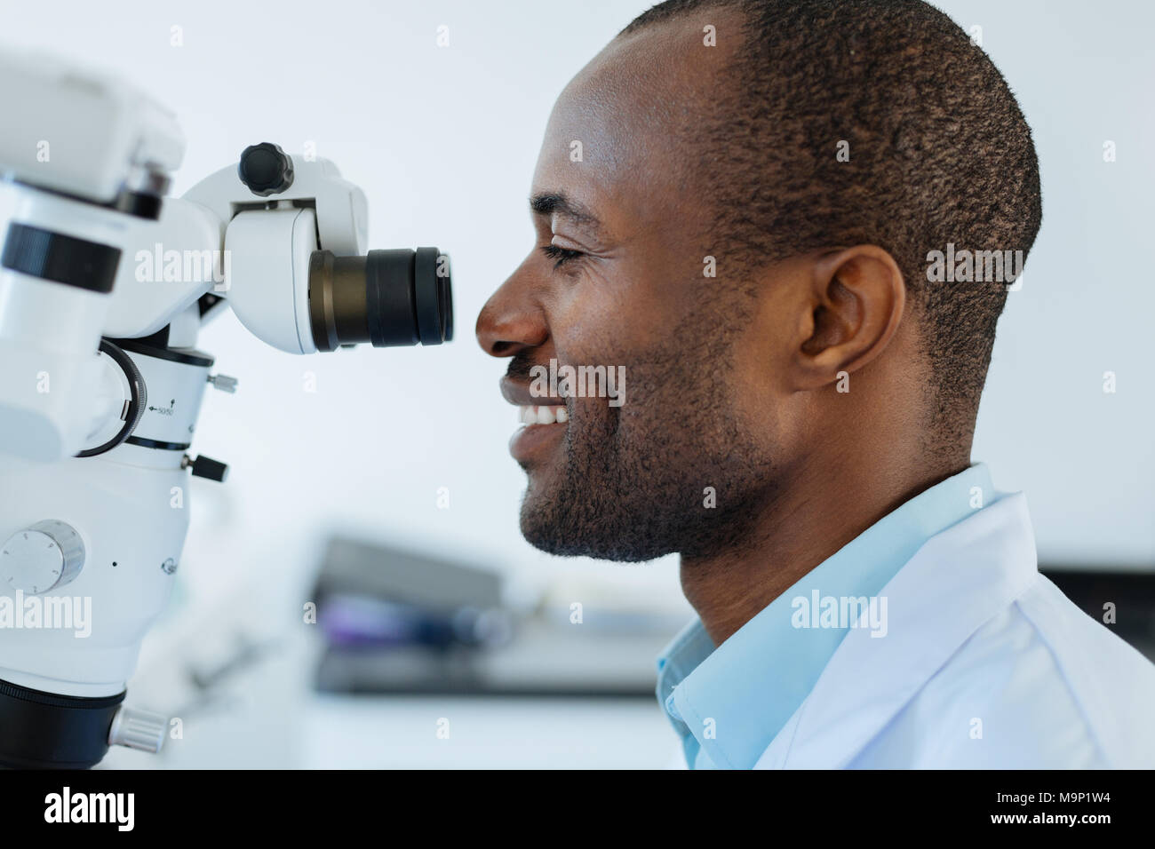 Cheerful dentist smiling while using microscope at work Stock Photo - Alamy