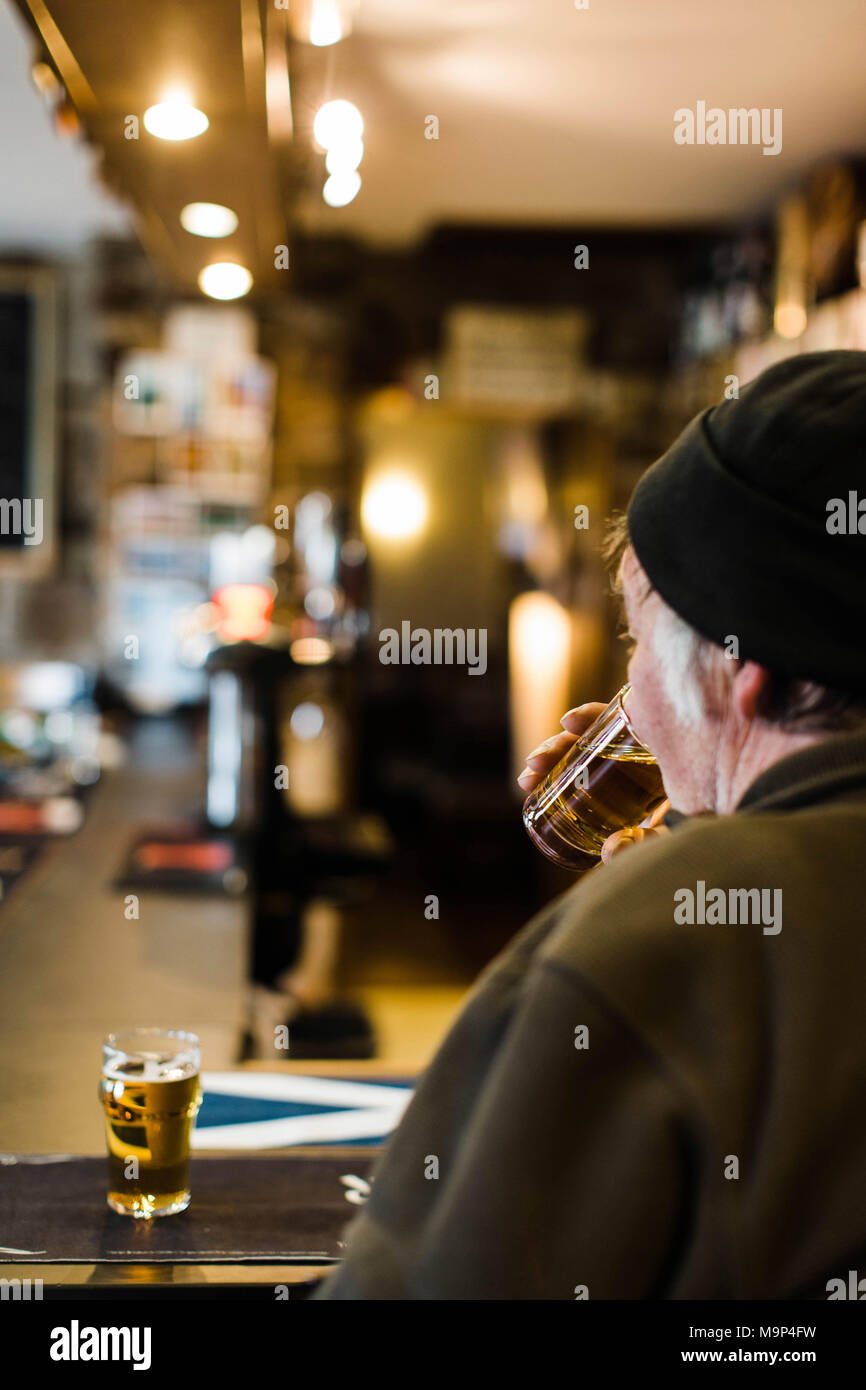 Rear view of older man enjoying glass of beer at pub, Scotland, UK ...