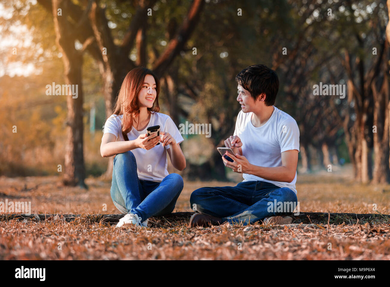 couple using mobile phone and talking in the park Stock Photo - Alamy