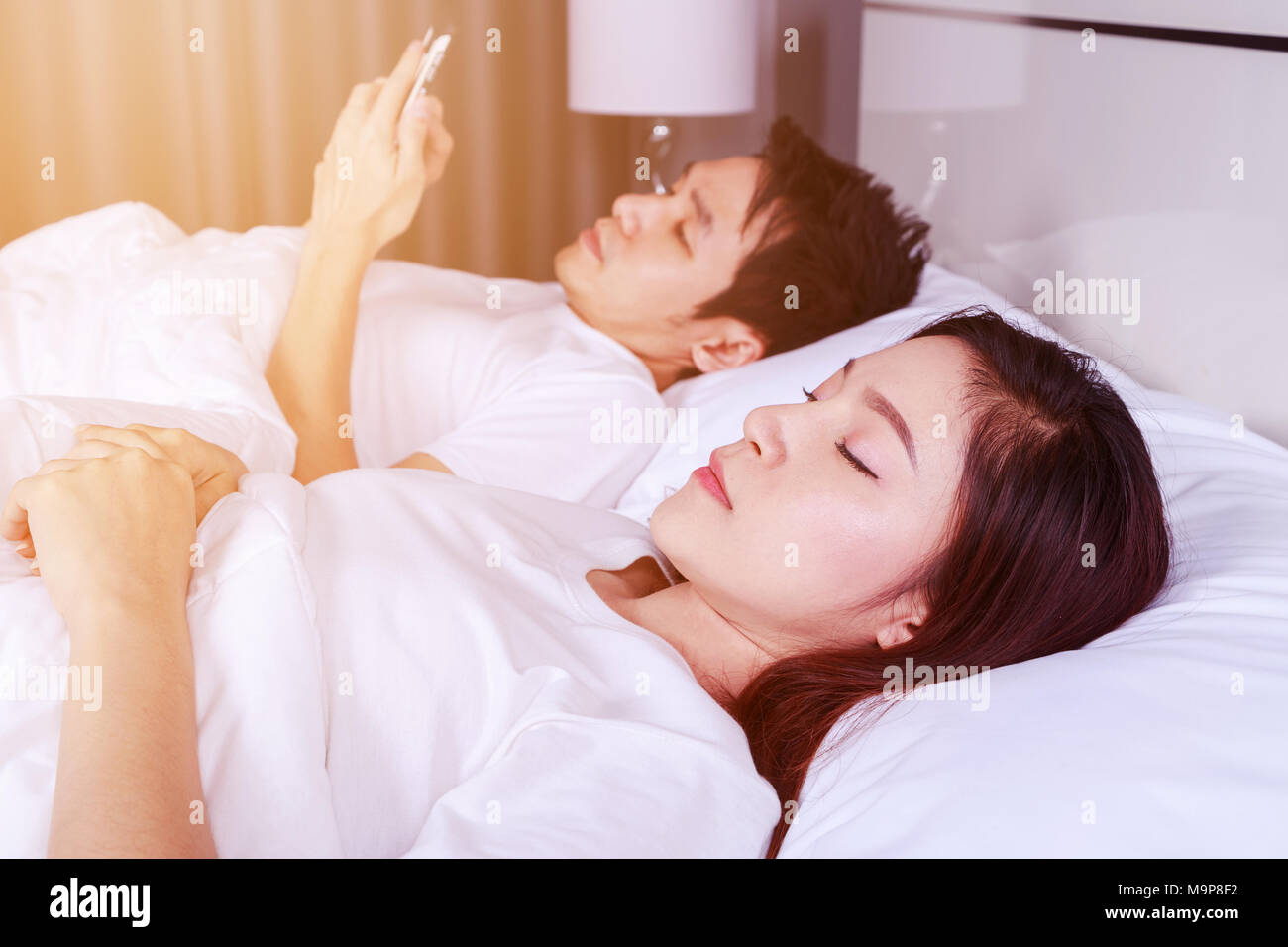 woman in bed with her sleeping and her husband texting on smartphone in ...