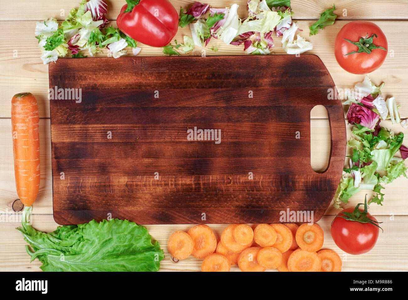 Frame of fresh vegetables around cutting board on wooden background ...