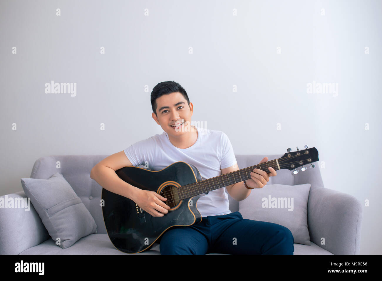 Handsome asian man playing on the guitar on the couch at home Stock ...