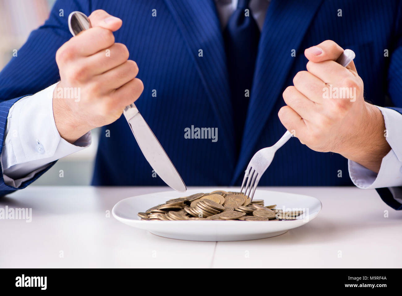 Funny businessman eating gold coins in office Stock Photo - Alamy