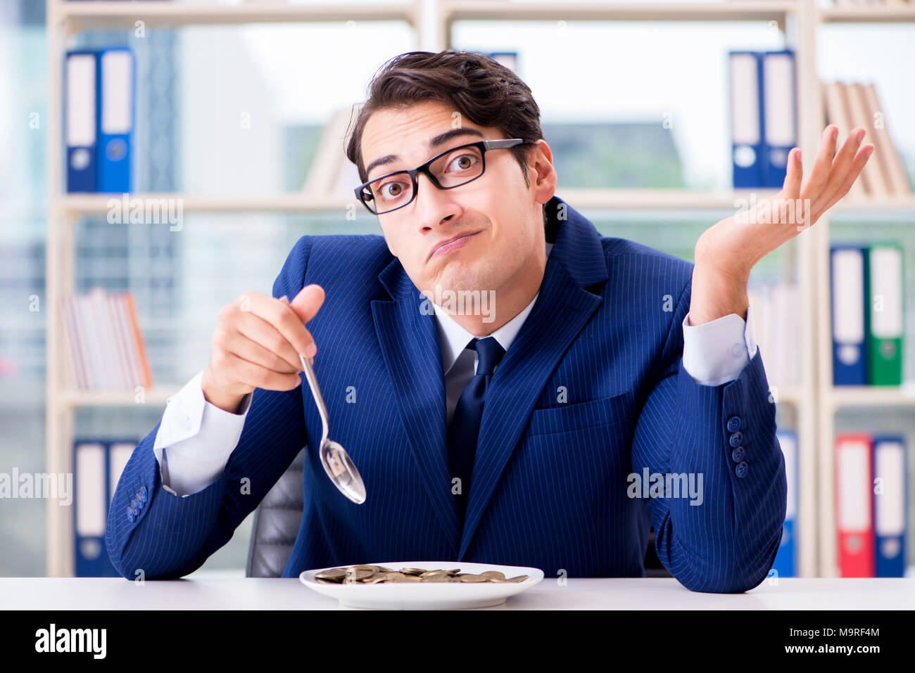 Funny businessman eating gold coins in office Stock Photo - Alamy