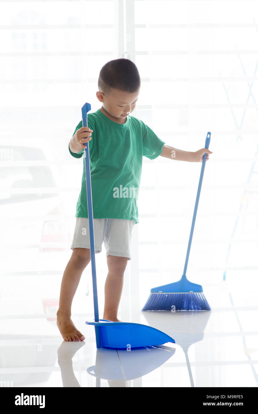 Young child doing house chores at home. Asian boy sweeping floor with ...